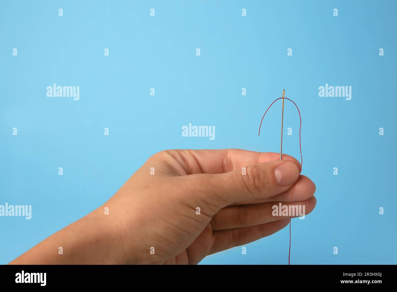 Woman holding sewing needle with thread on light blue background ...