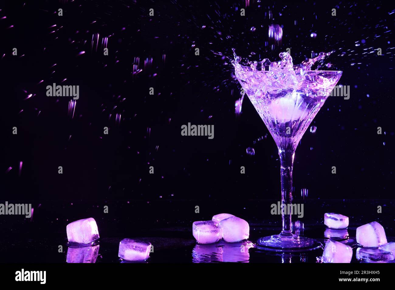 Glass of martini with ice and splashes in neon lights on dark ...