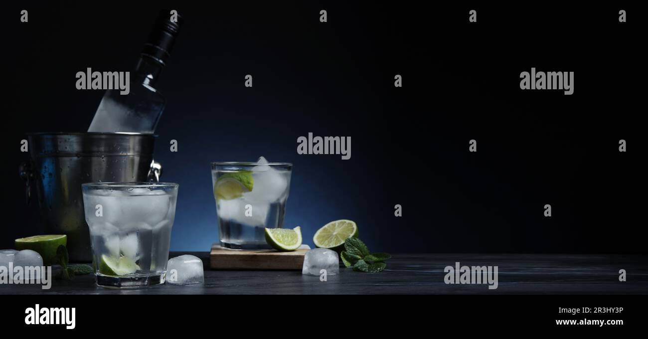 Bottle of vodka, glasses, lime, mint and ice on black marble table ...