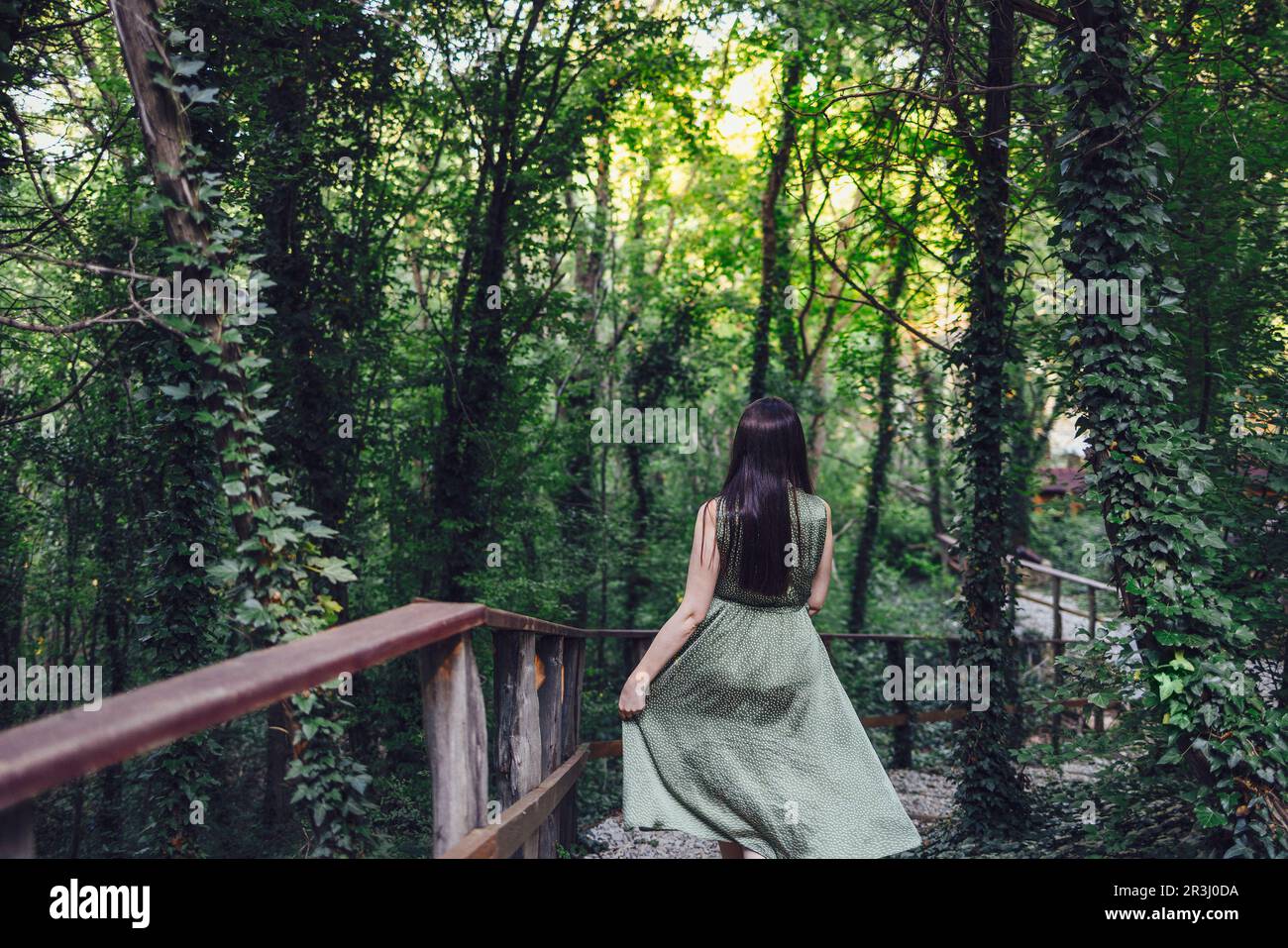 Charming young woman with long hair stands on path in forest and looks ...