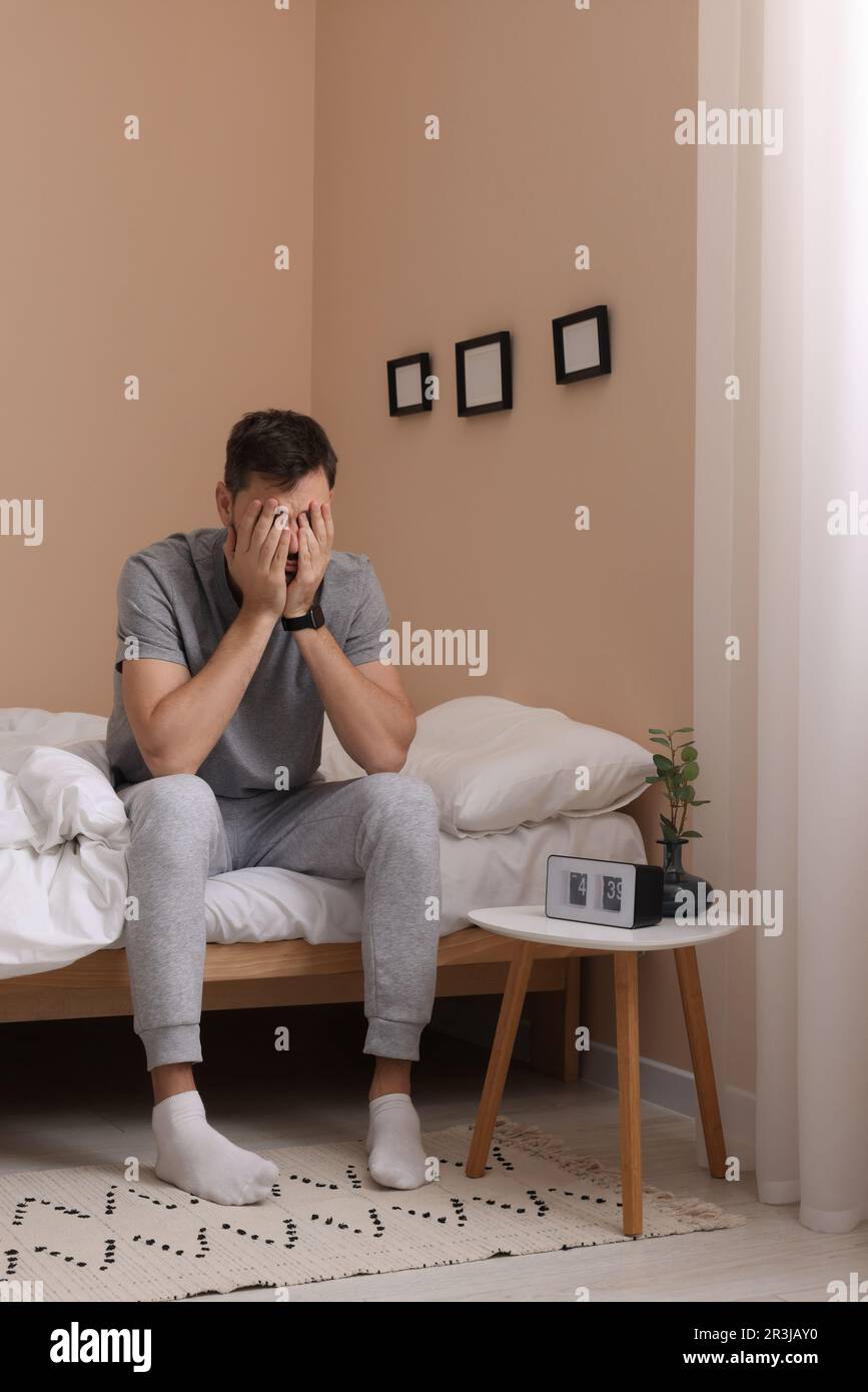 Sleepy man covering his face with hands on bed at home Stock Photo - Alamy