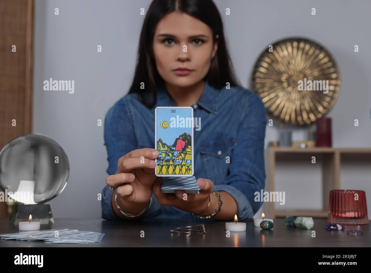 Fortune teller with tarot card Eight of Cups at grey table indoors ...