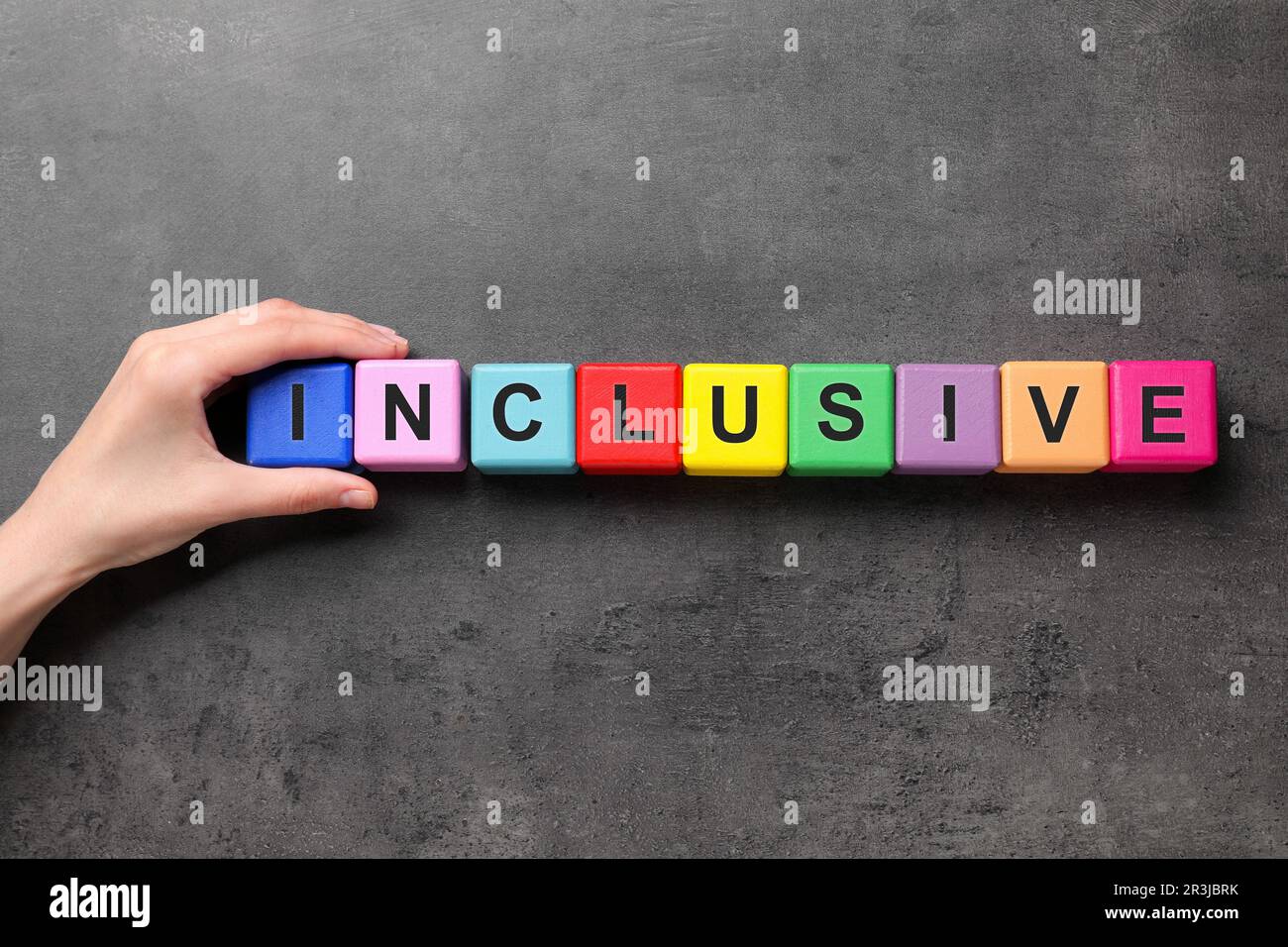 Woman making word Inclusive with cubes on dark grey background, top ...