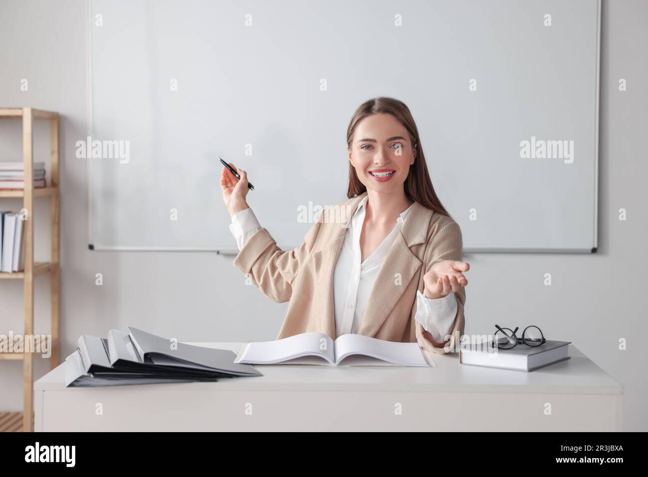 Happy young teacher explaining something at table in classroom Stock ...