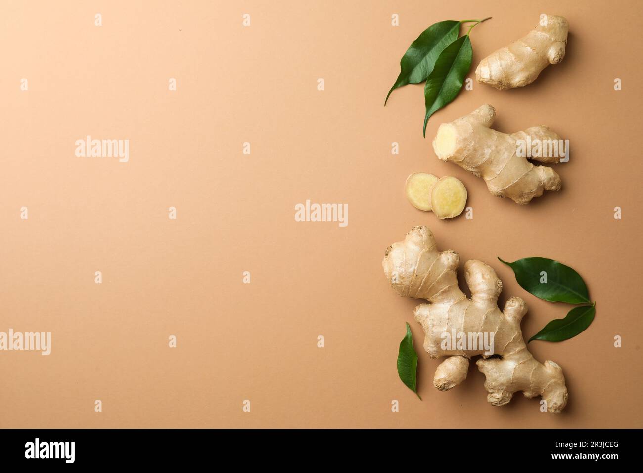 Fresh ginger with green leaves on light pale brown background, flat lay ...