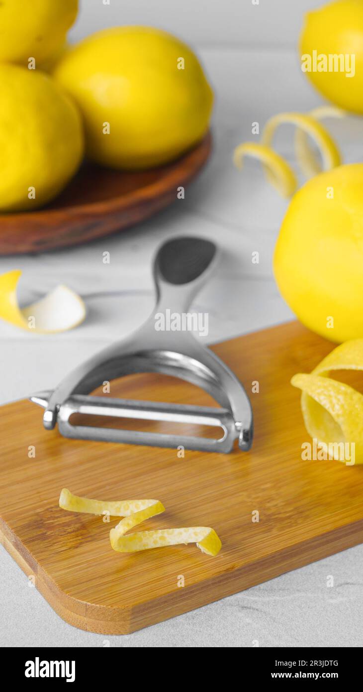 Wooden board, lemons, peeler and fresh rind on white textured table ...