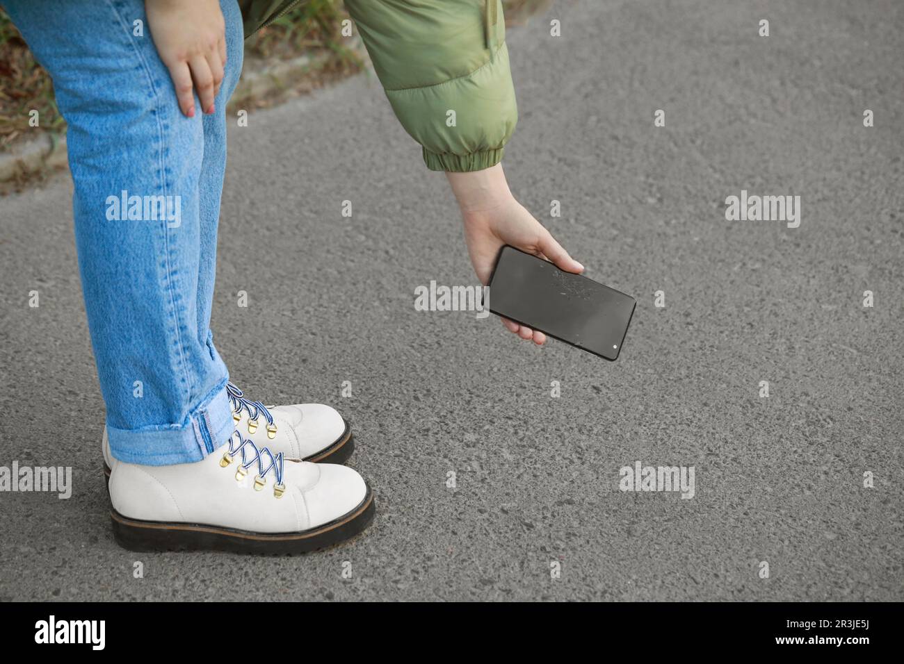 Woman taking dropped smartphone from asphalt outdoors, closeup. Device ...