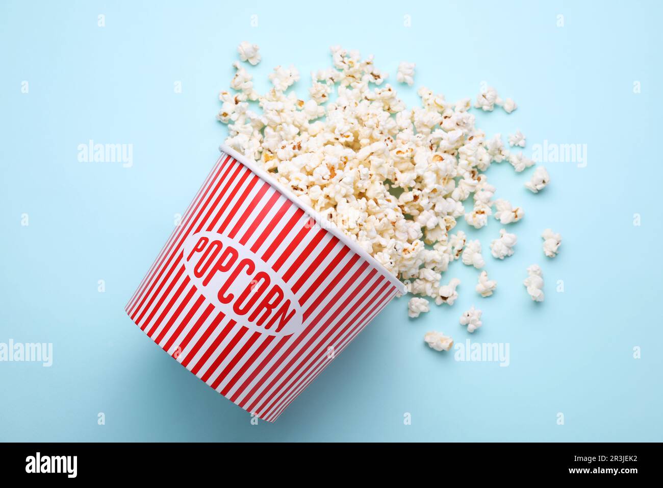 Overturned paper bucket with delicious popcorn on light blue background ...