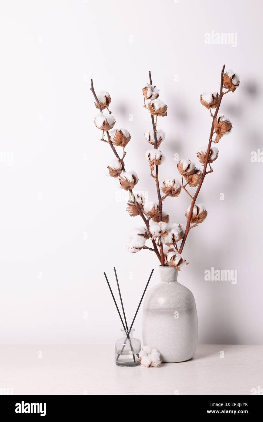 Reed diffuser and vase with cotton branches on table against white ...