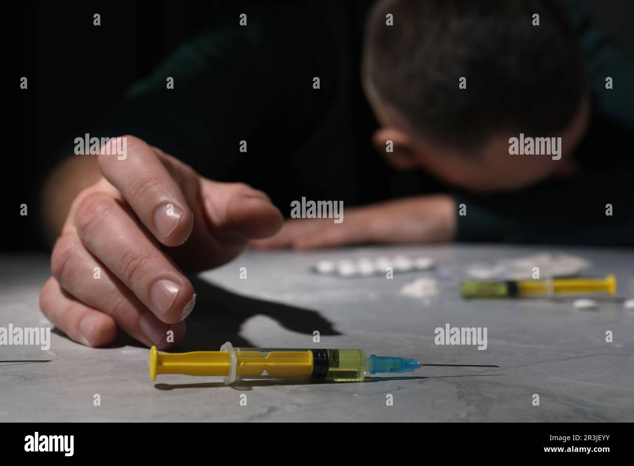 Overdosed man at grey table, focus on syringe with drugs Stock Photo ...