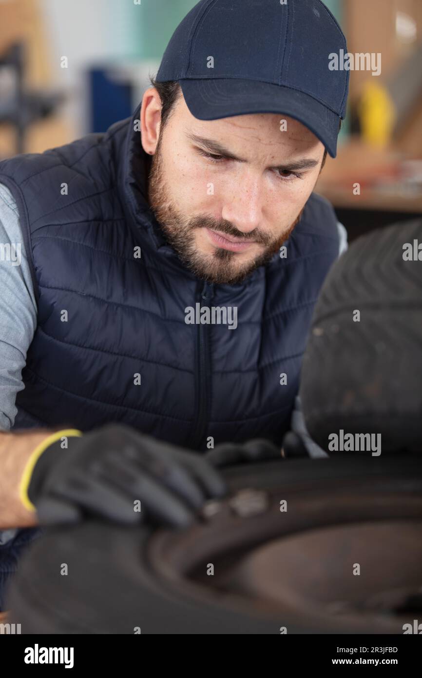 young mechanic with blue uniform checking black tyre Stock Photo - Alamy