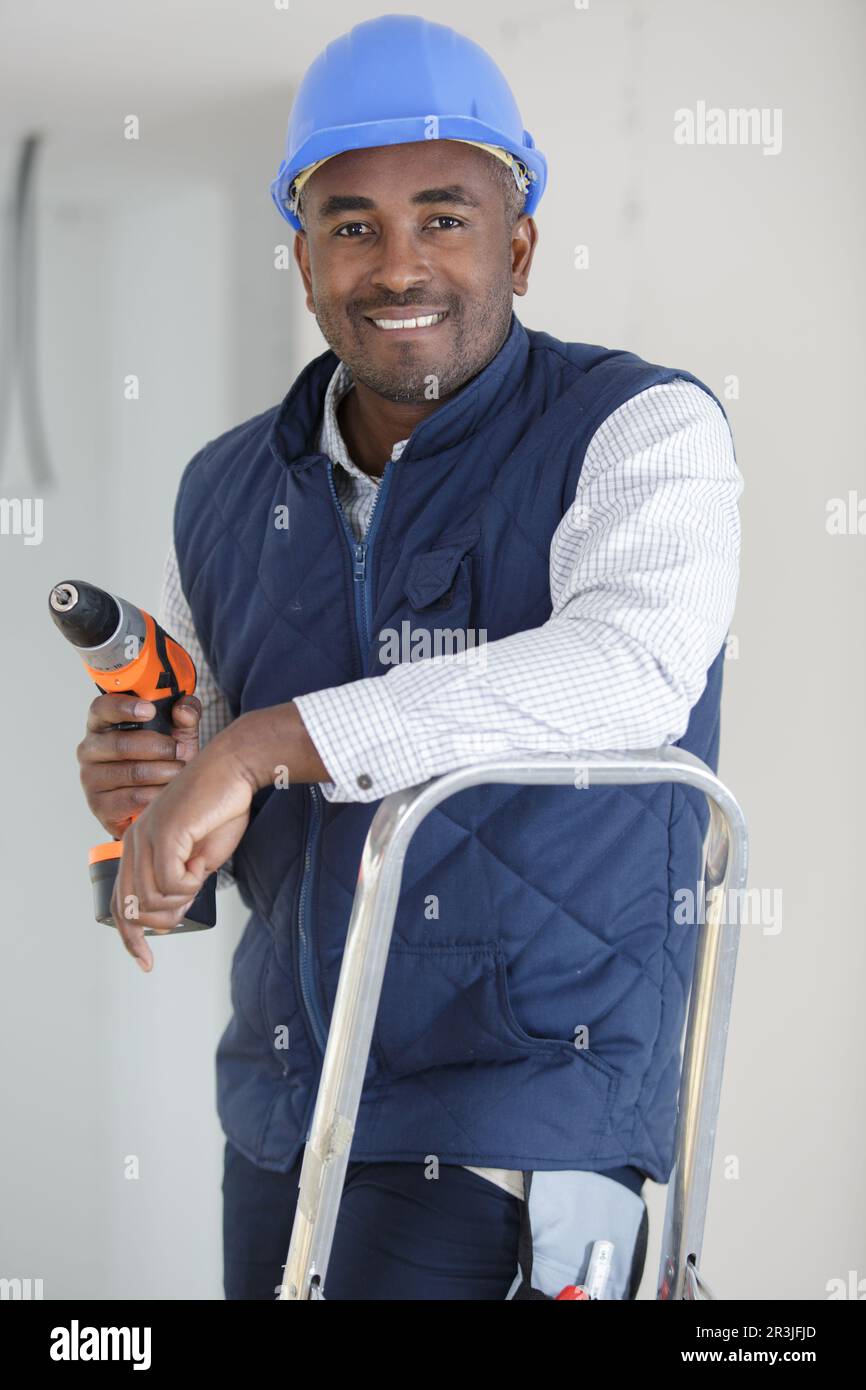 happy male builder standing on ladder with drill Stock Photo - Alamy