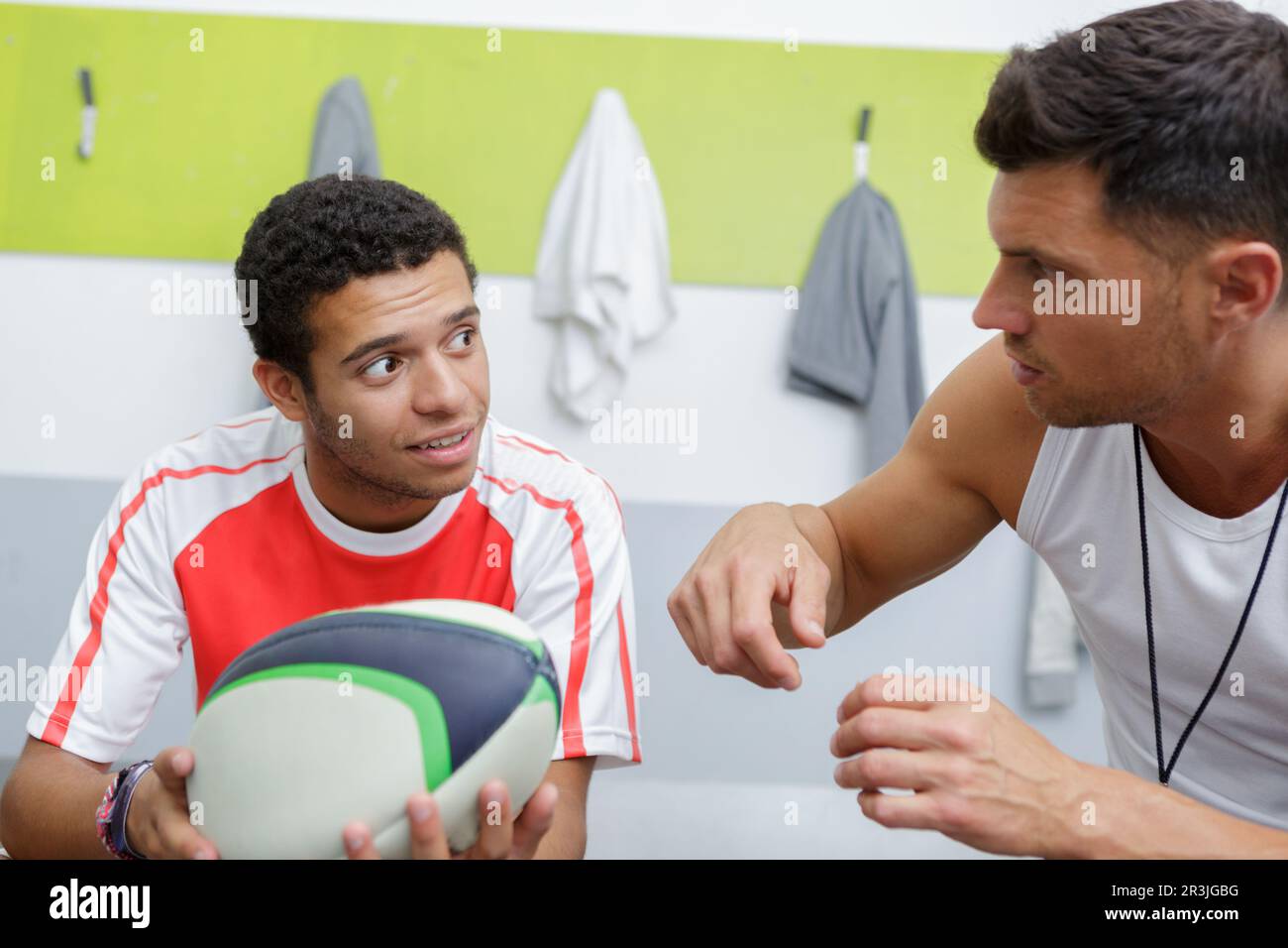 young man holding rugby ball talking to coach Stock Photo - Alamy