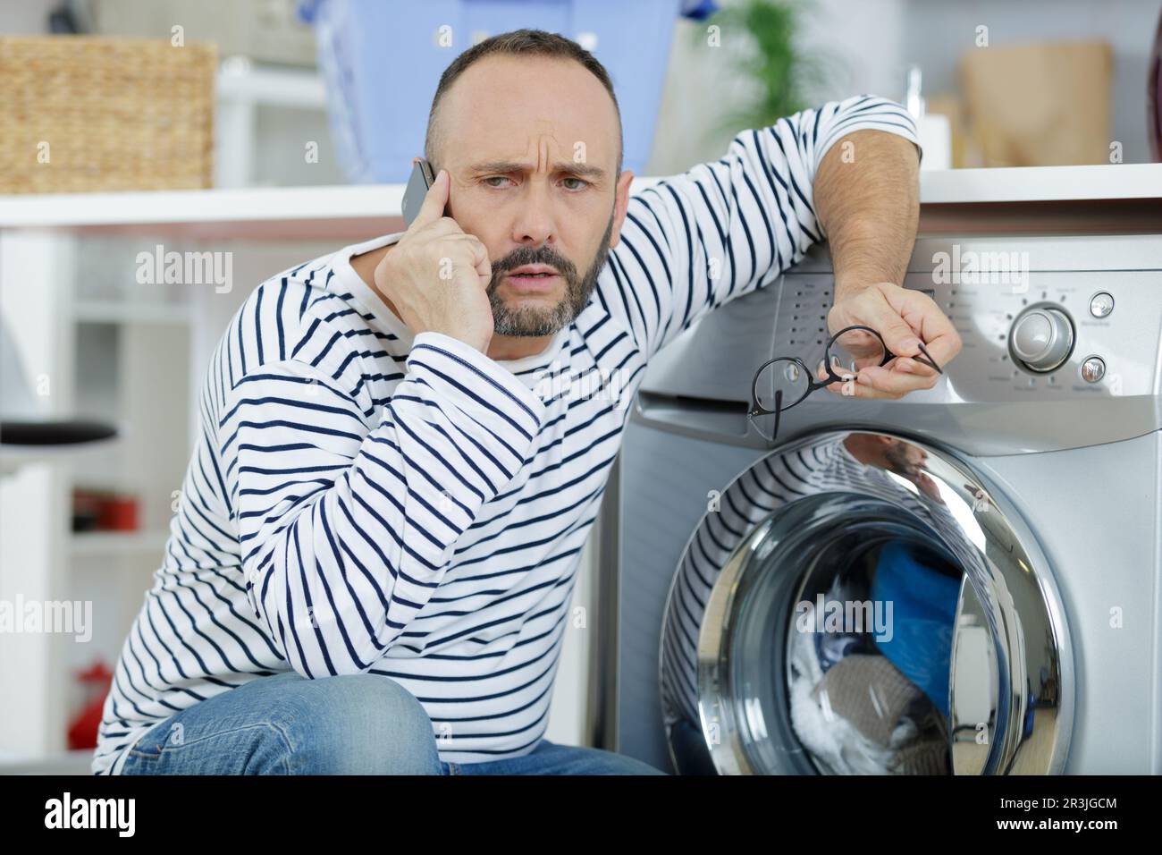 man making telephone call crouched beside washing machine Stock Photo ...