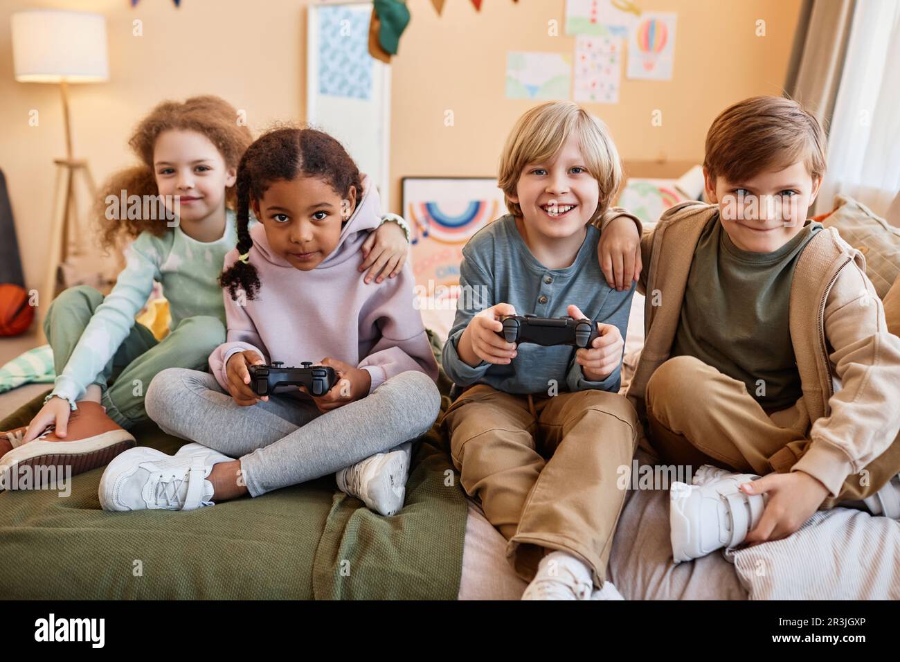 Diverse group of happy little children playing video games together and ...