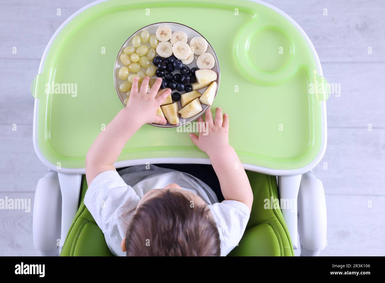 Cute little baby eating healthy food in high chair indoors, top view ...