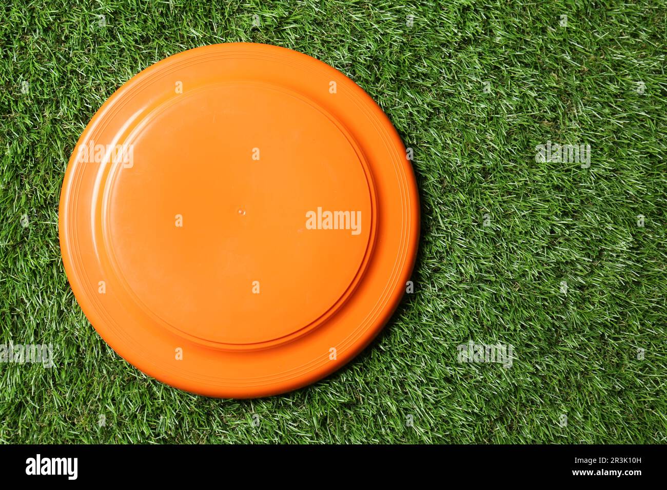 Orange plastic frisbee disk on green grass, top view. Space for text ...