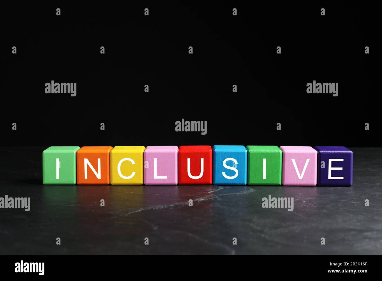 Colorful cubes with word Inclusive on marble table against black ...