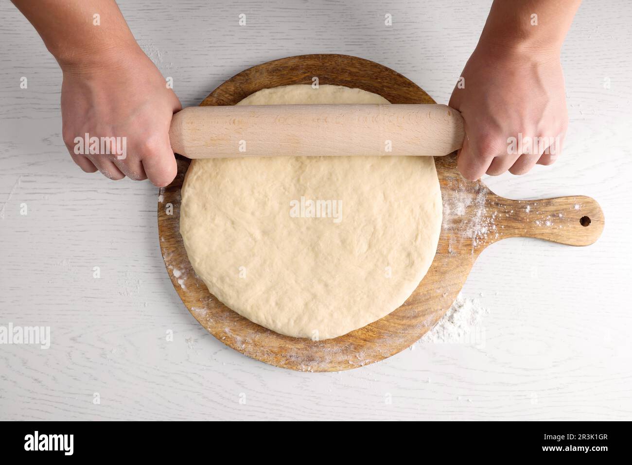 Man rolling dough with wooden pin at white table, top view Stock Photo ...