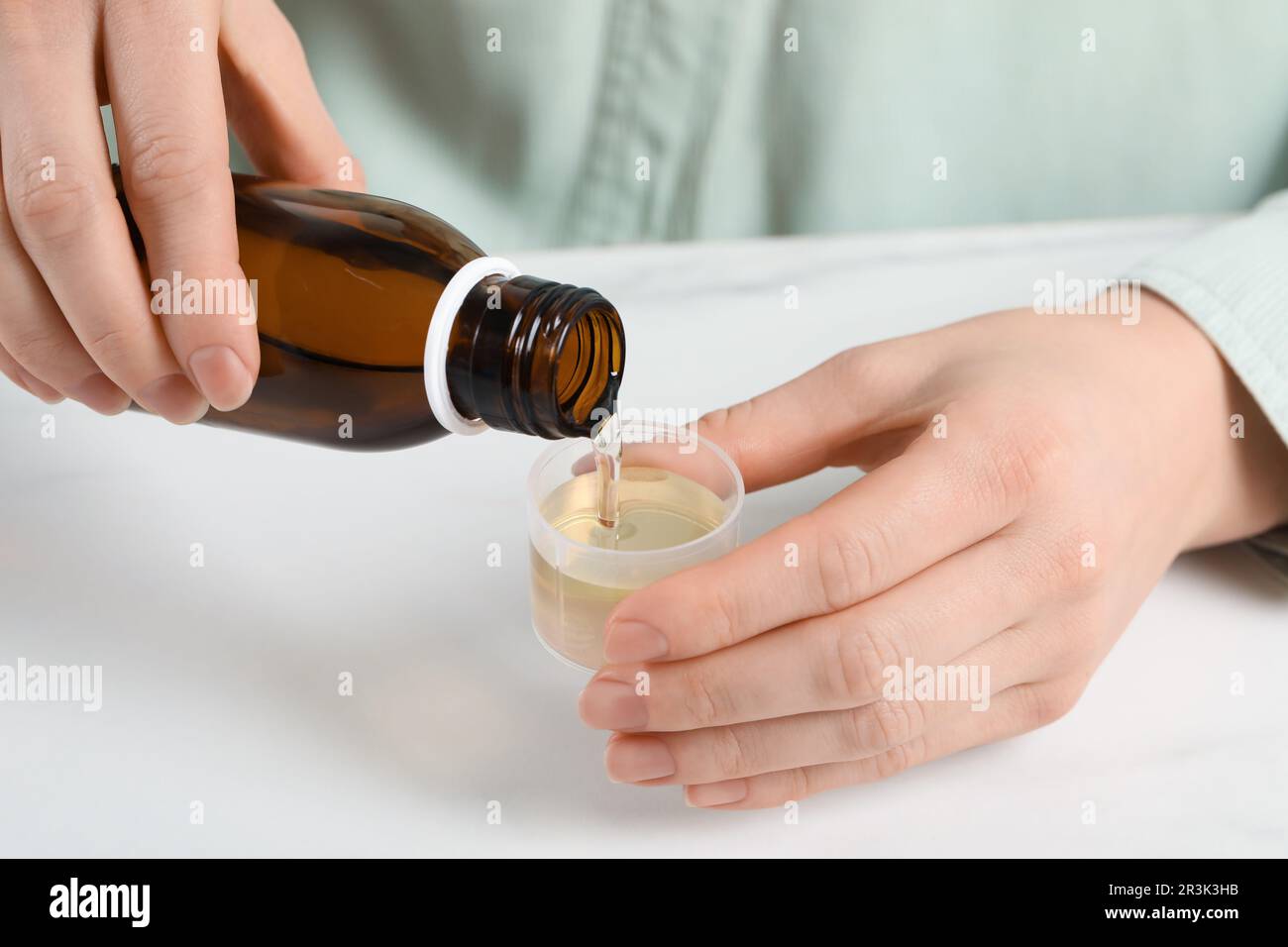 Woman pouring syrup from bottle into measuring cup at white table ...