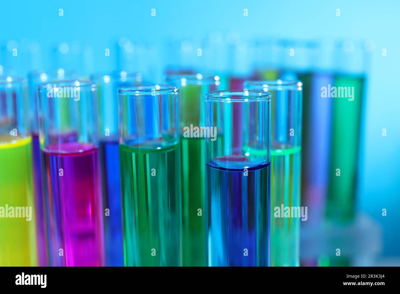 Many test tubes with colorful liquids on light blue background, closeup ...