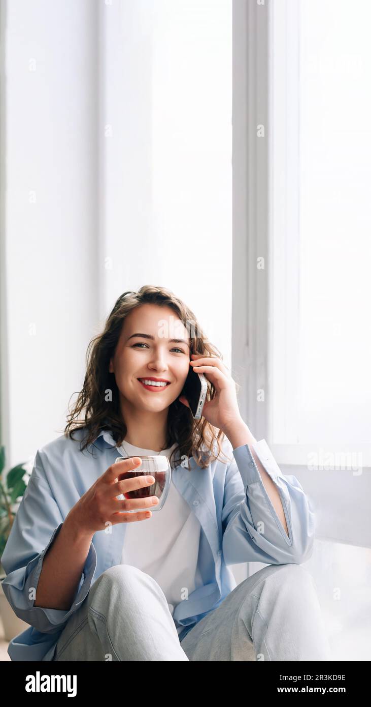 Adorable cute funny woman with a mug of black tea talking on the phone ...