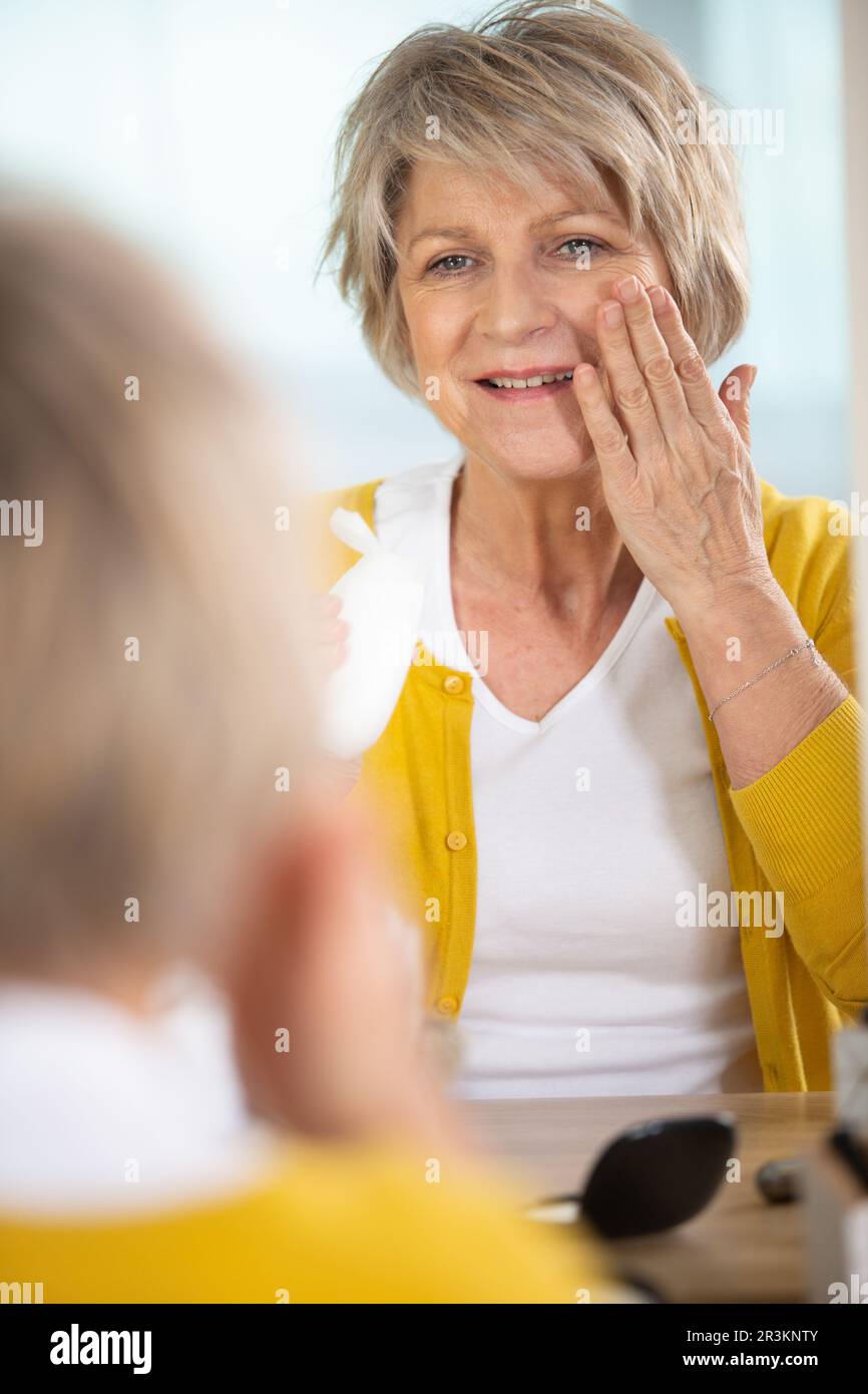 elderly woman applying moisturiser to her cheek Stock Photo - Alamy