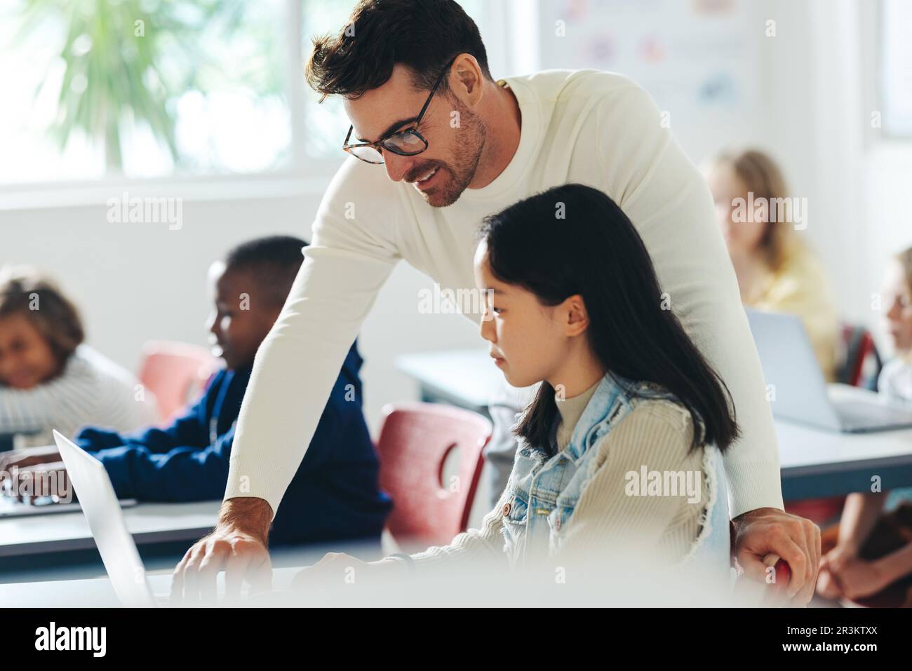 Primary school educator assisting a student with coding and programming lessons in a digital ...