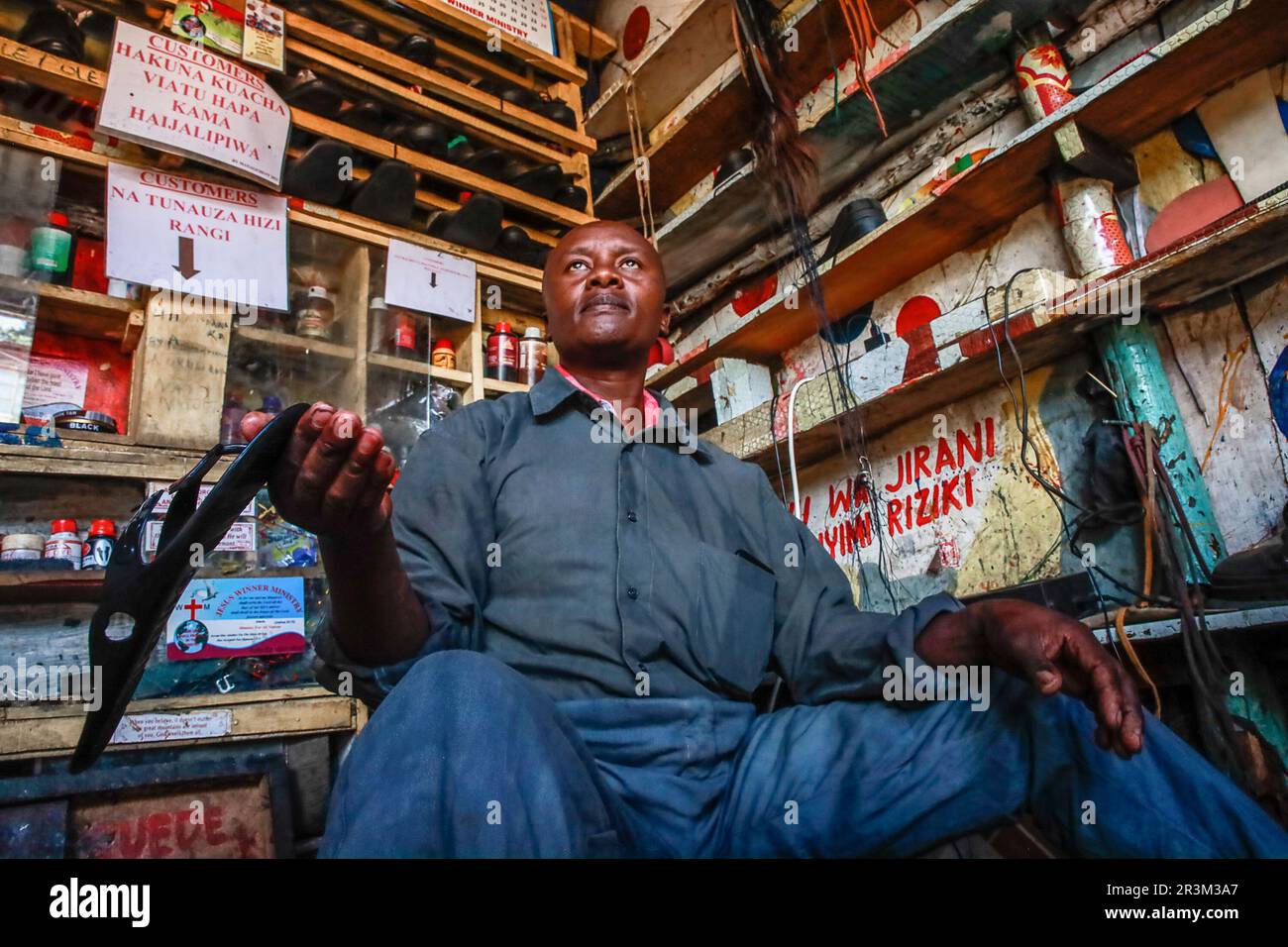 Daniel Mwangi, a local cobbler repairing a customer's shoe at his shop ...