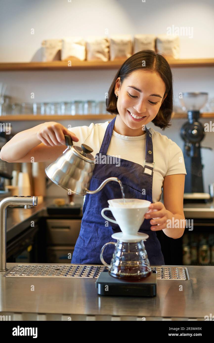 Vertical shot of smiling asian bartender, barista in blue apron ...