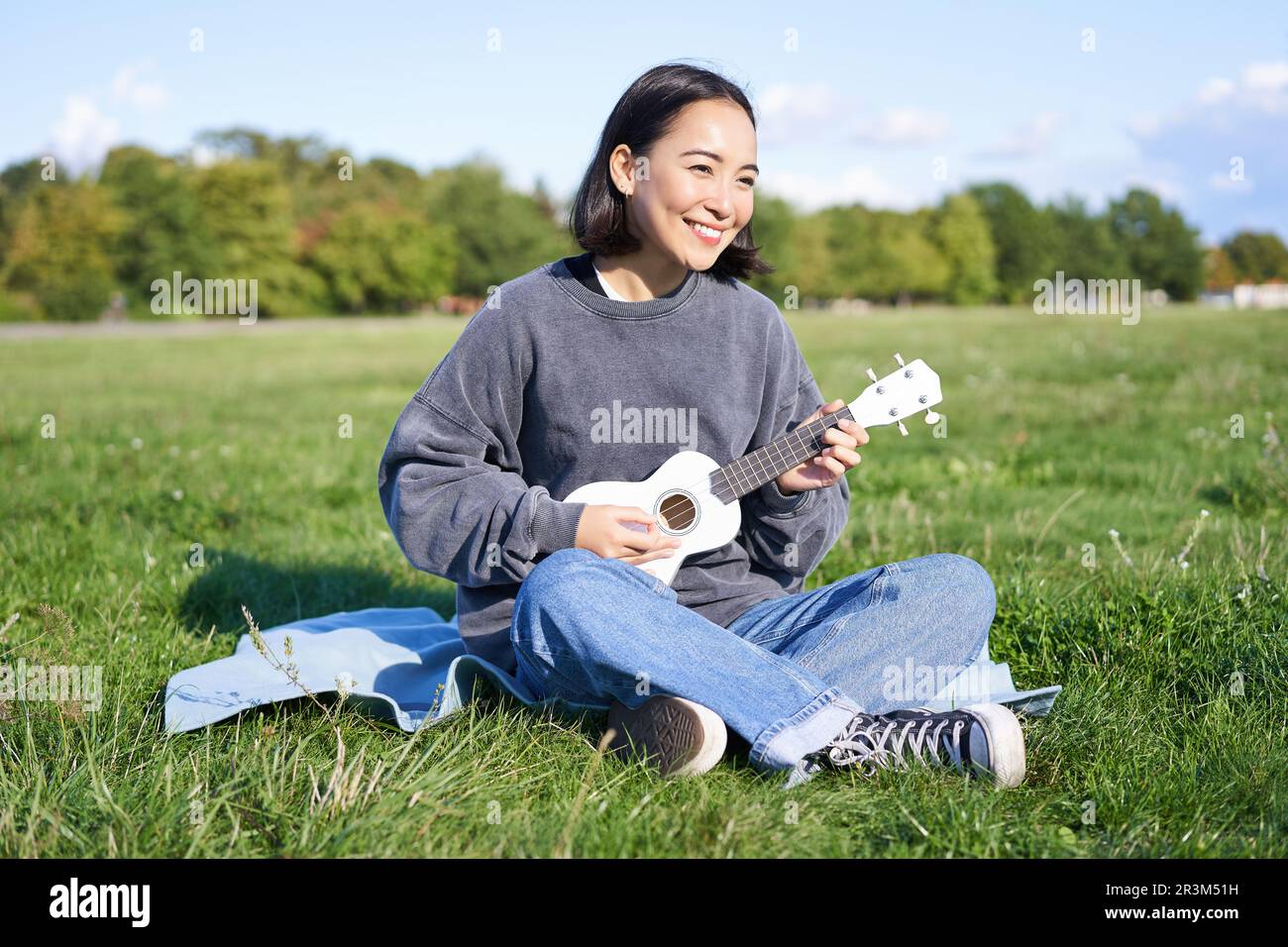 Beautiful asian girl sitting in park, playing ukulele and singing ...