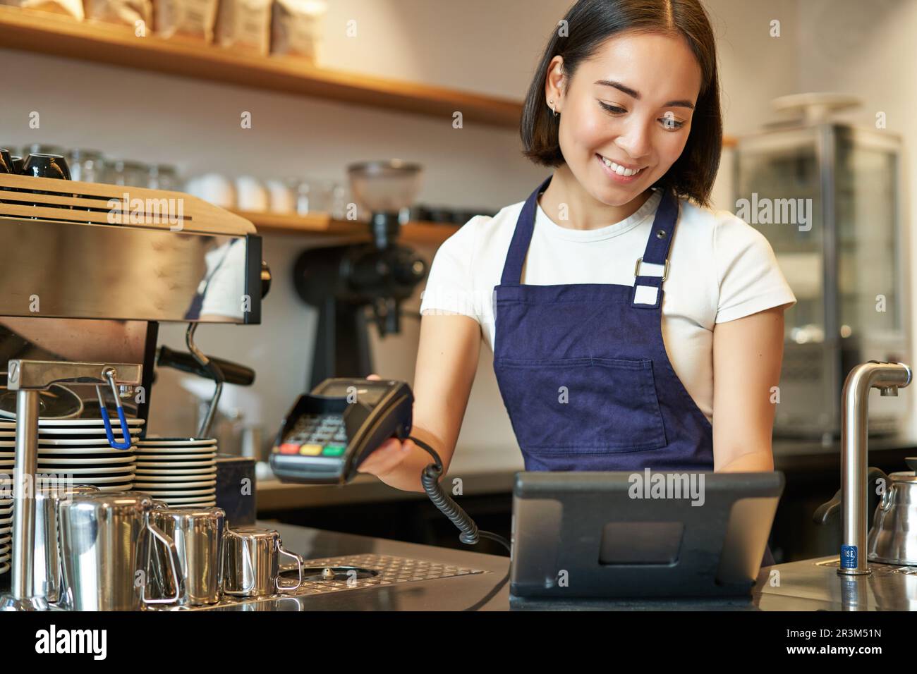 Smiling asian barista girl processing order, enter order in POS ...