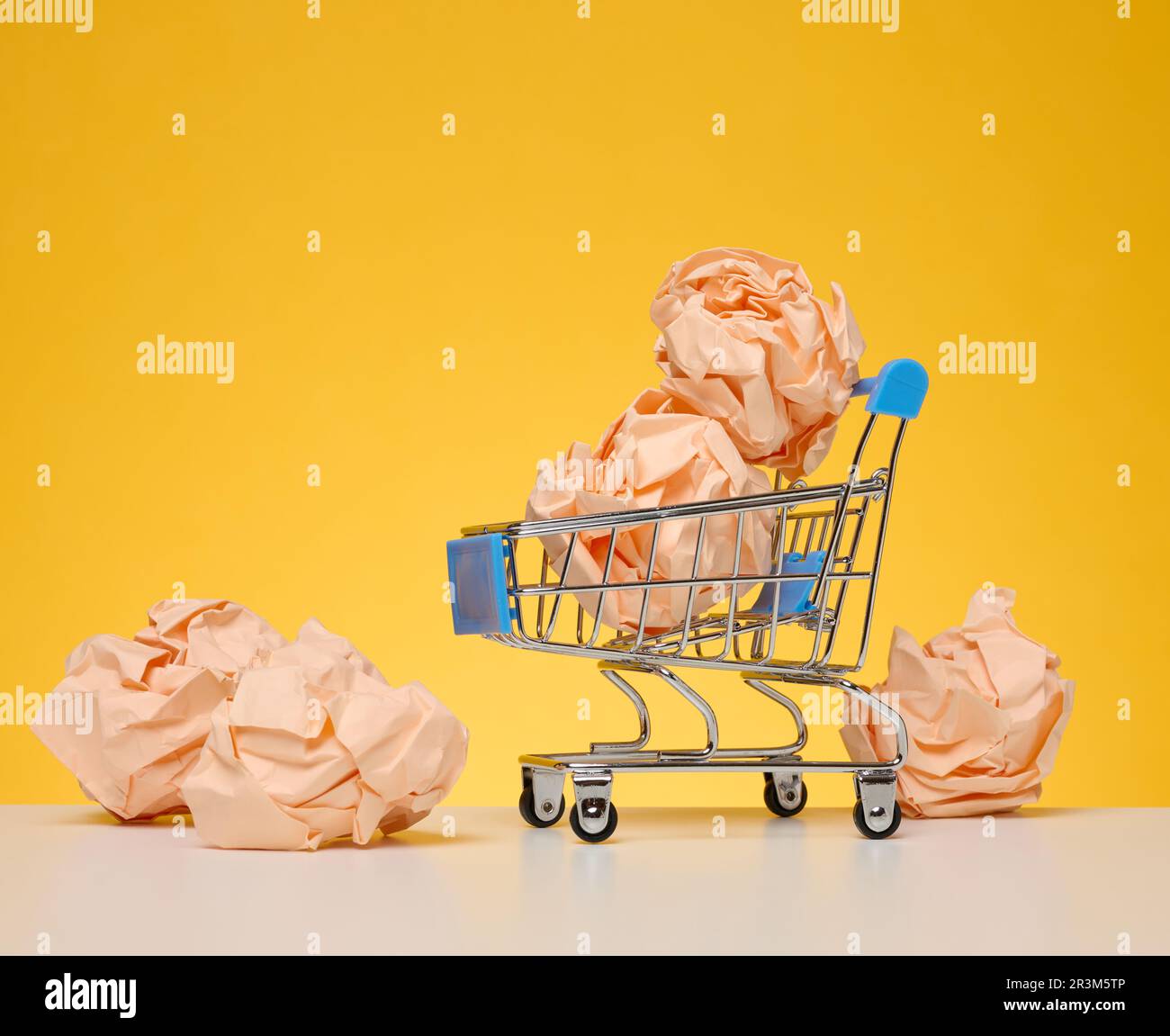 Crumpled balls of paper in a miniature shopping cart on a yellow ...