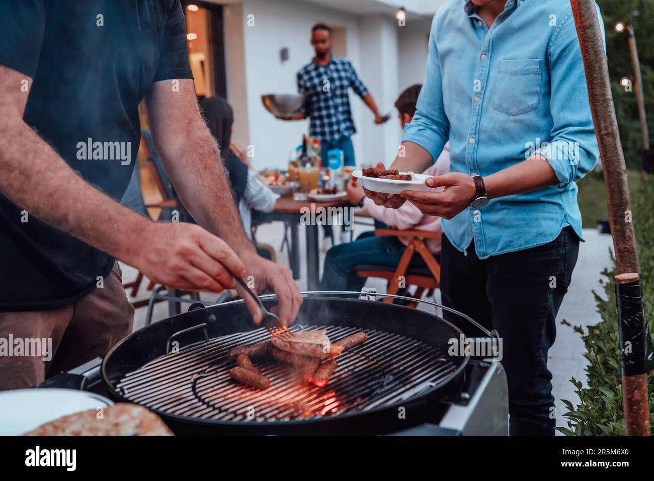 A group of friends and family barbecue together in the evening on the ...