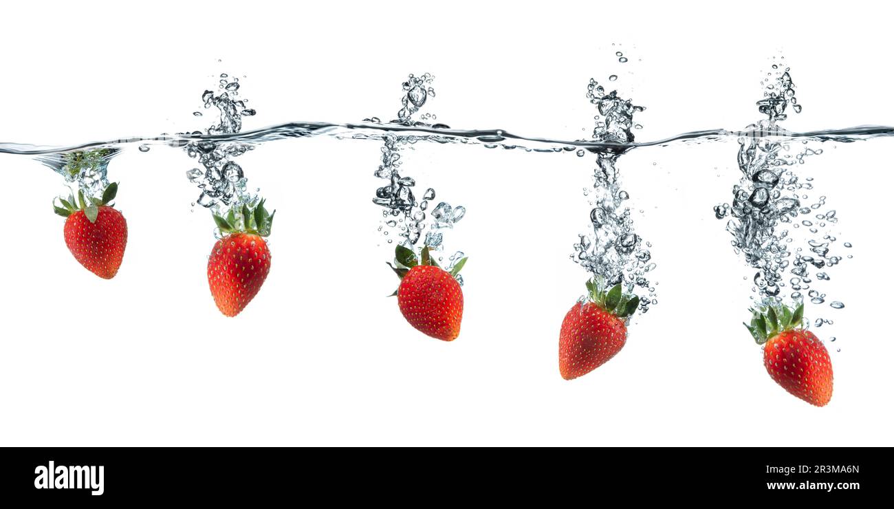 Multiple vibrant red strawberries dropping into crystal clear water ...