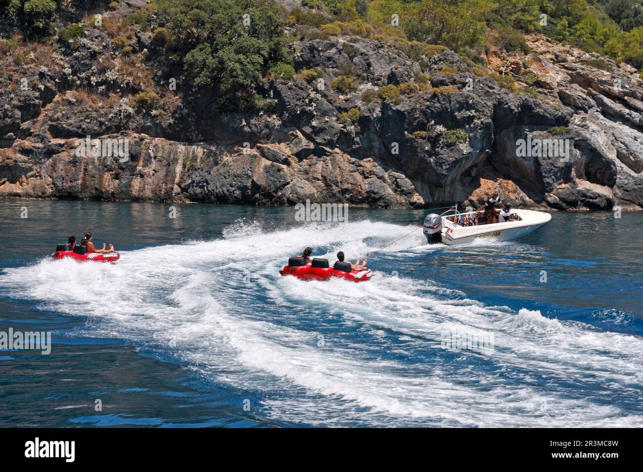 people in 2 large red inflatables, pulled by motorboat through water ...