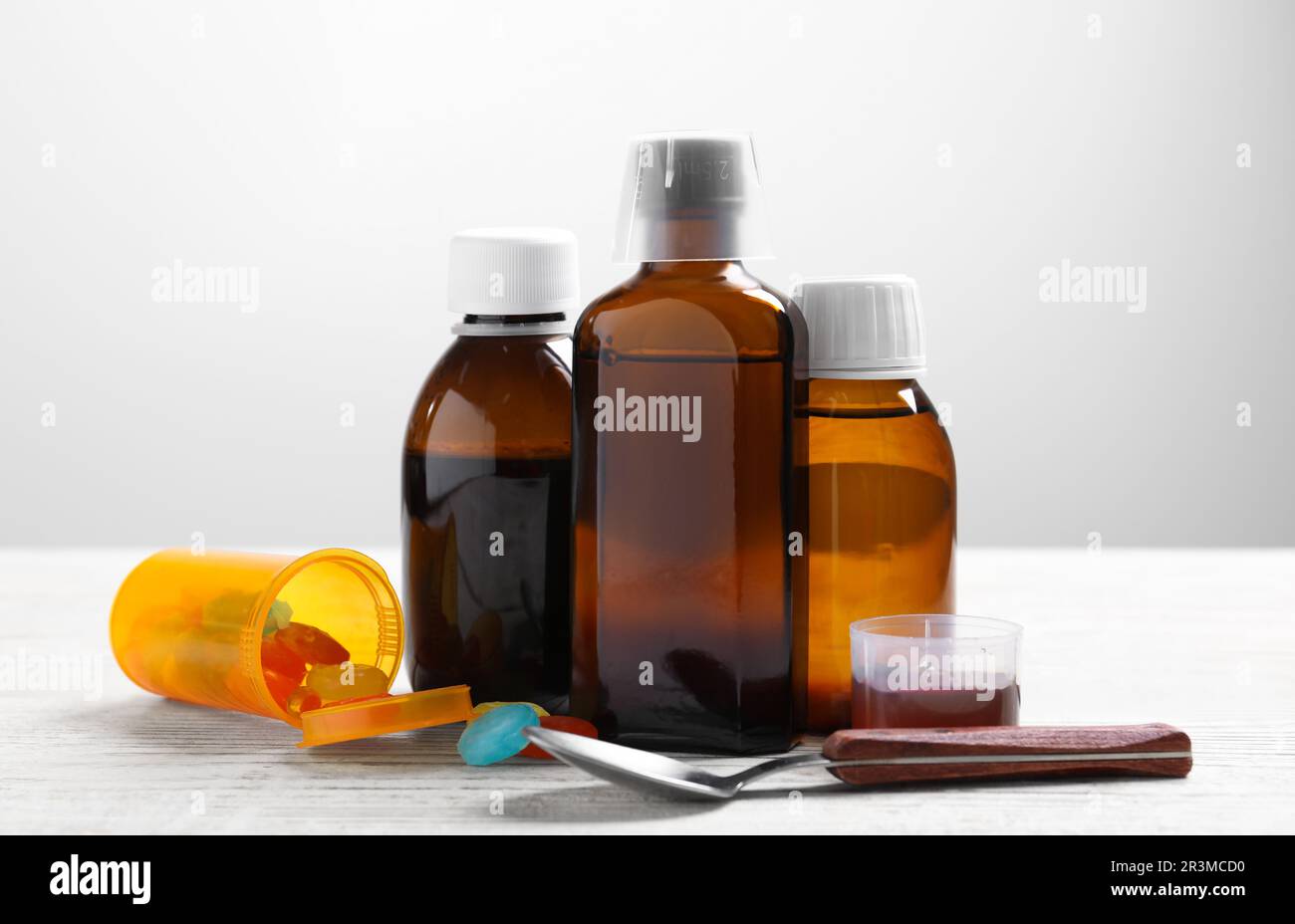 Bottles of syrup, measuring cup, lozenges and spoon on white wooden ...