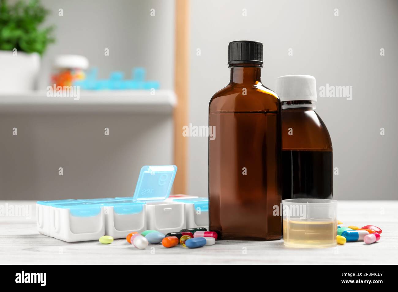Bottles of syrup, measuring cup, weekly pill organizer and pills on ...