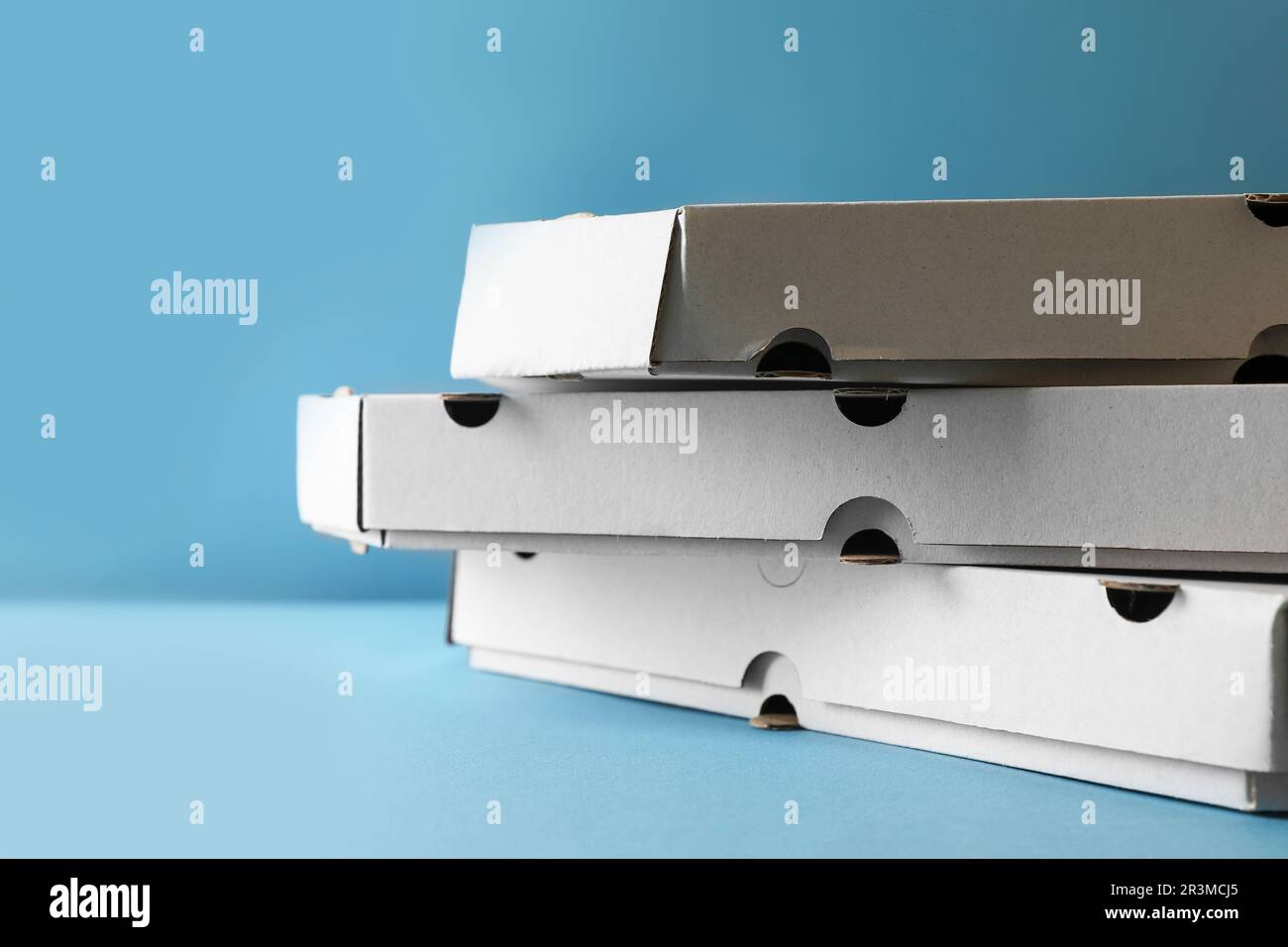 Stack of empty pizza boxes on light blue background, closeup. Space for ...