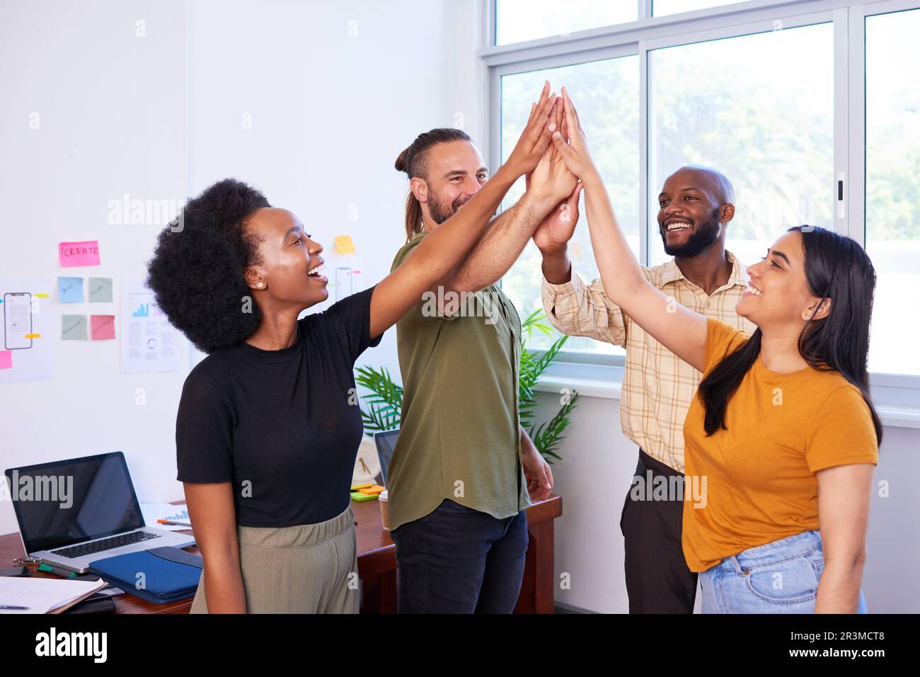 Four diverse team members give high five, celebrate success in creative ...