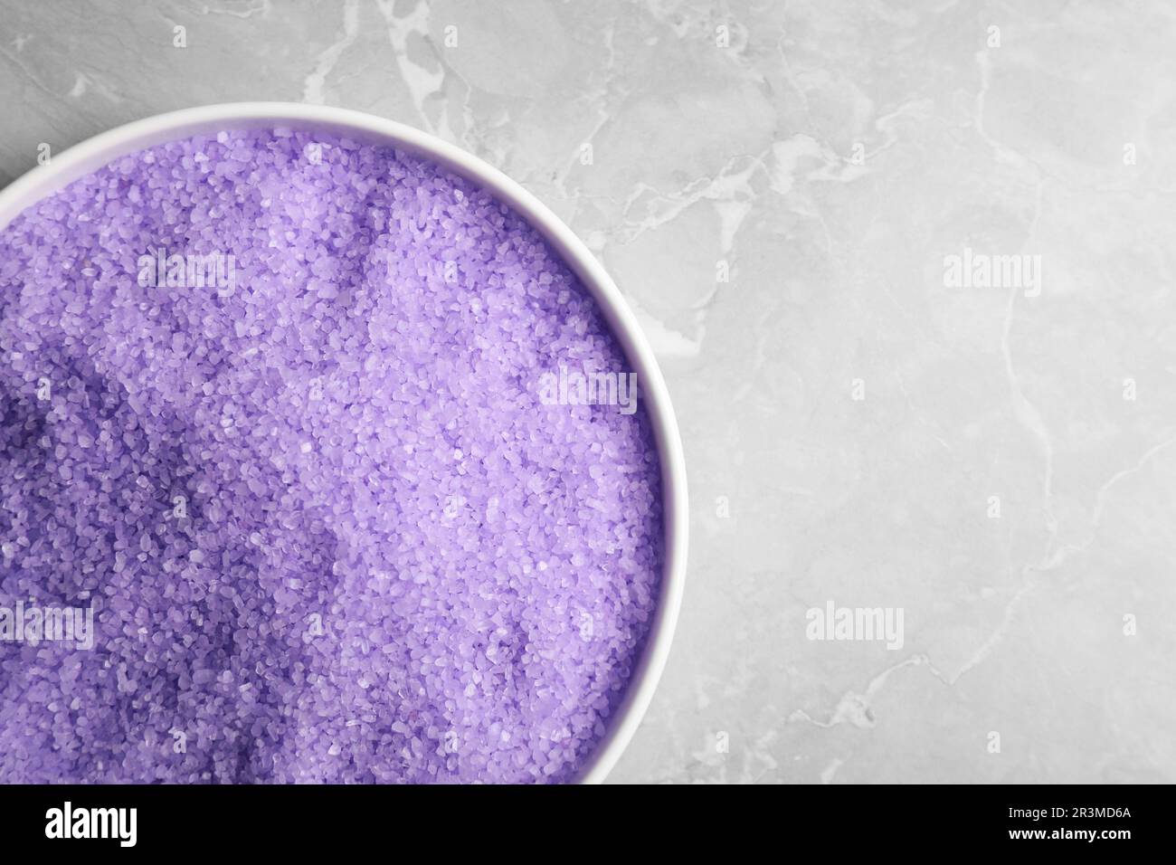 Plate with purple sea salt on grey marble table, top view. Space for ...