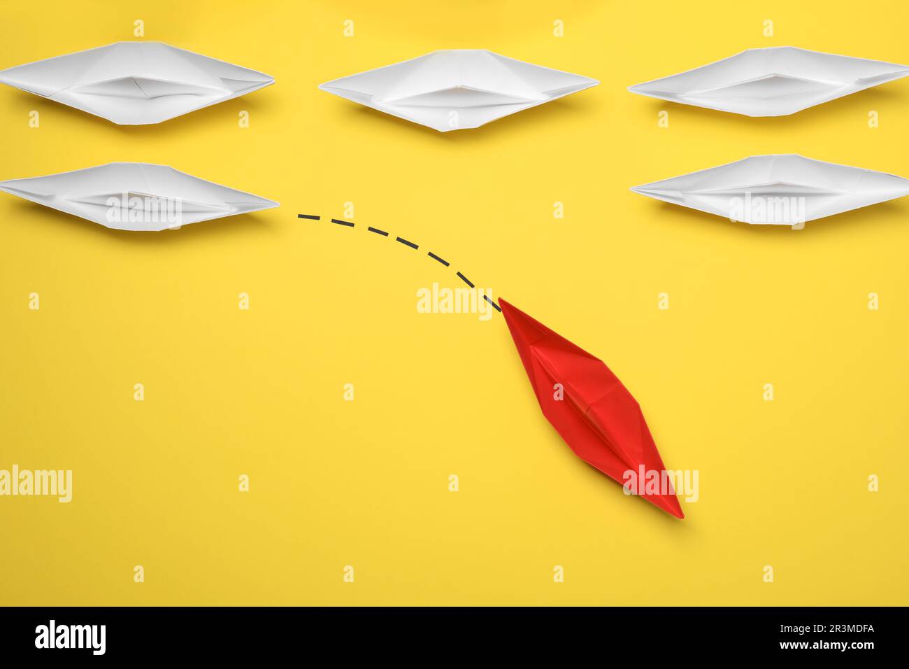 Red paper boat floating away from others on yellow background, flat lay ...