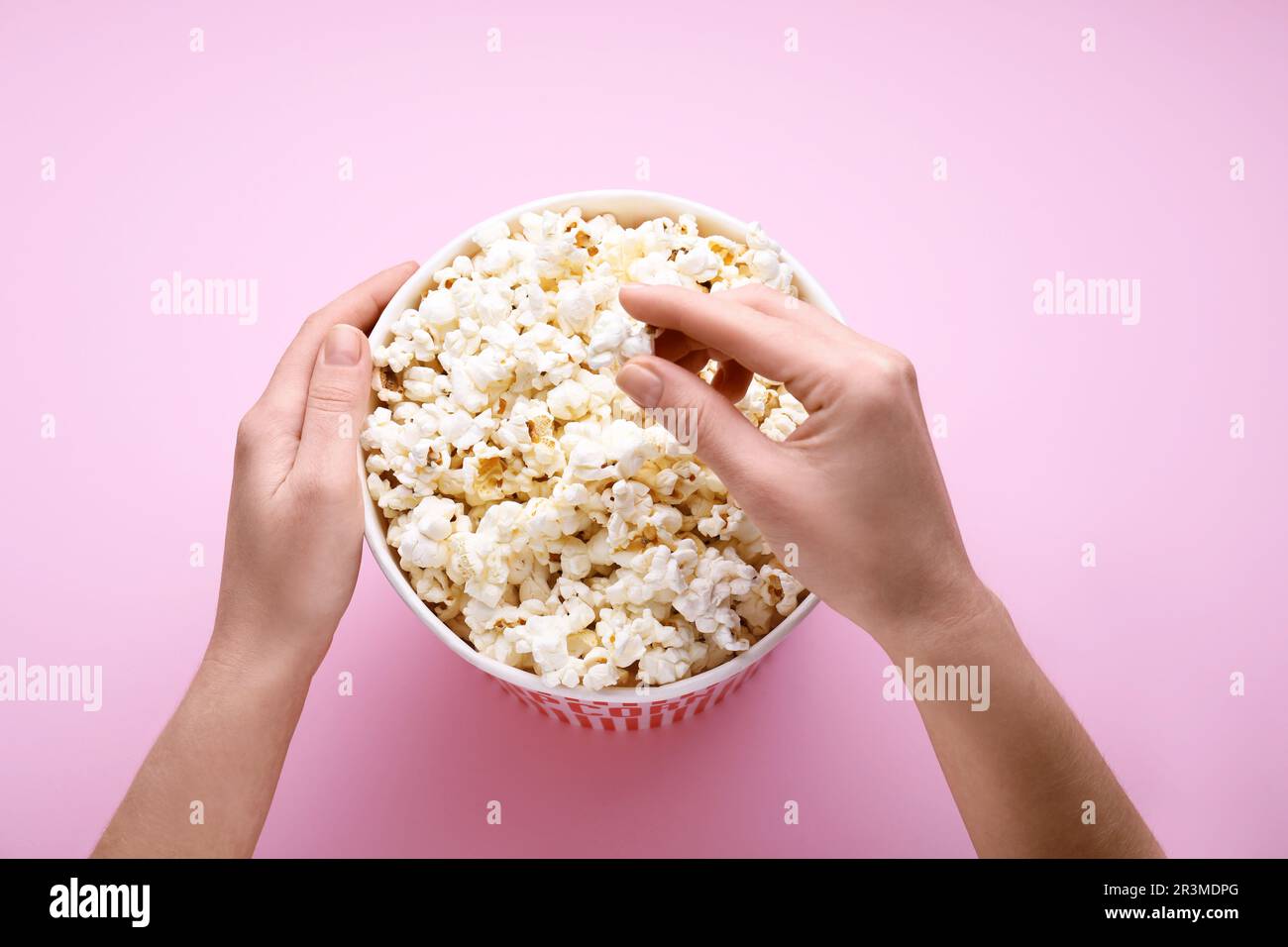 Woman taking fresh popcorn from bucket on pink background, above view ...
