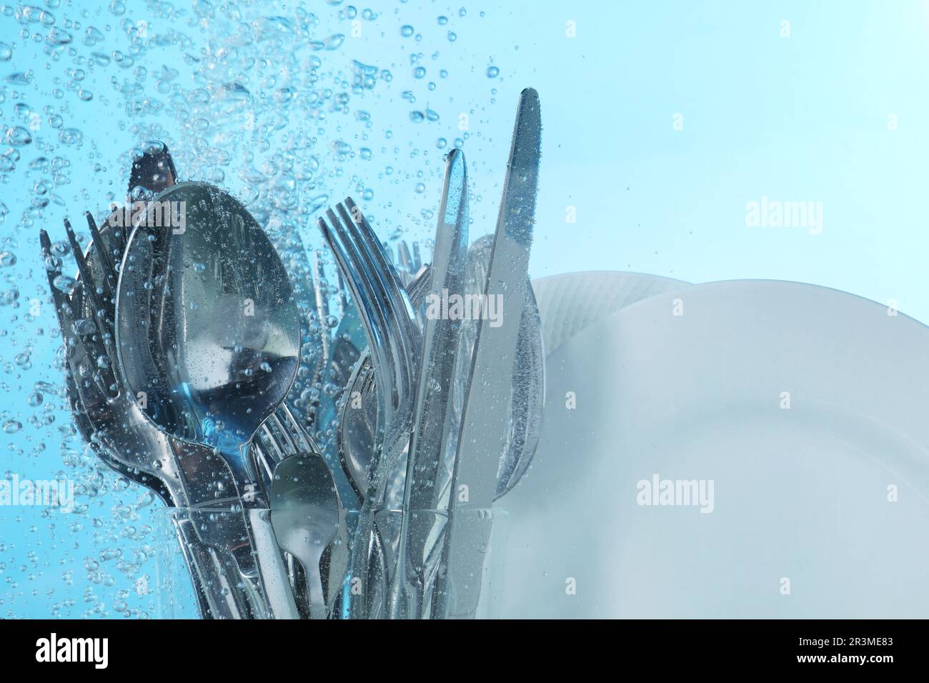 Washing silver cutlery and plates in water on light blue background ...