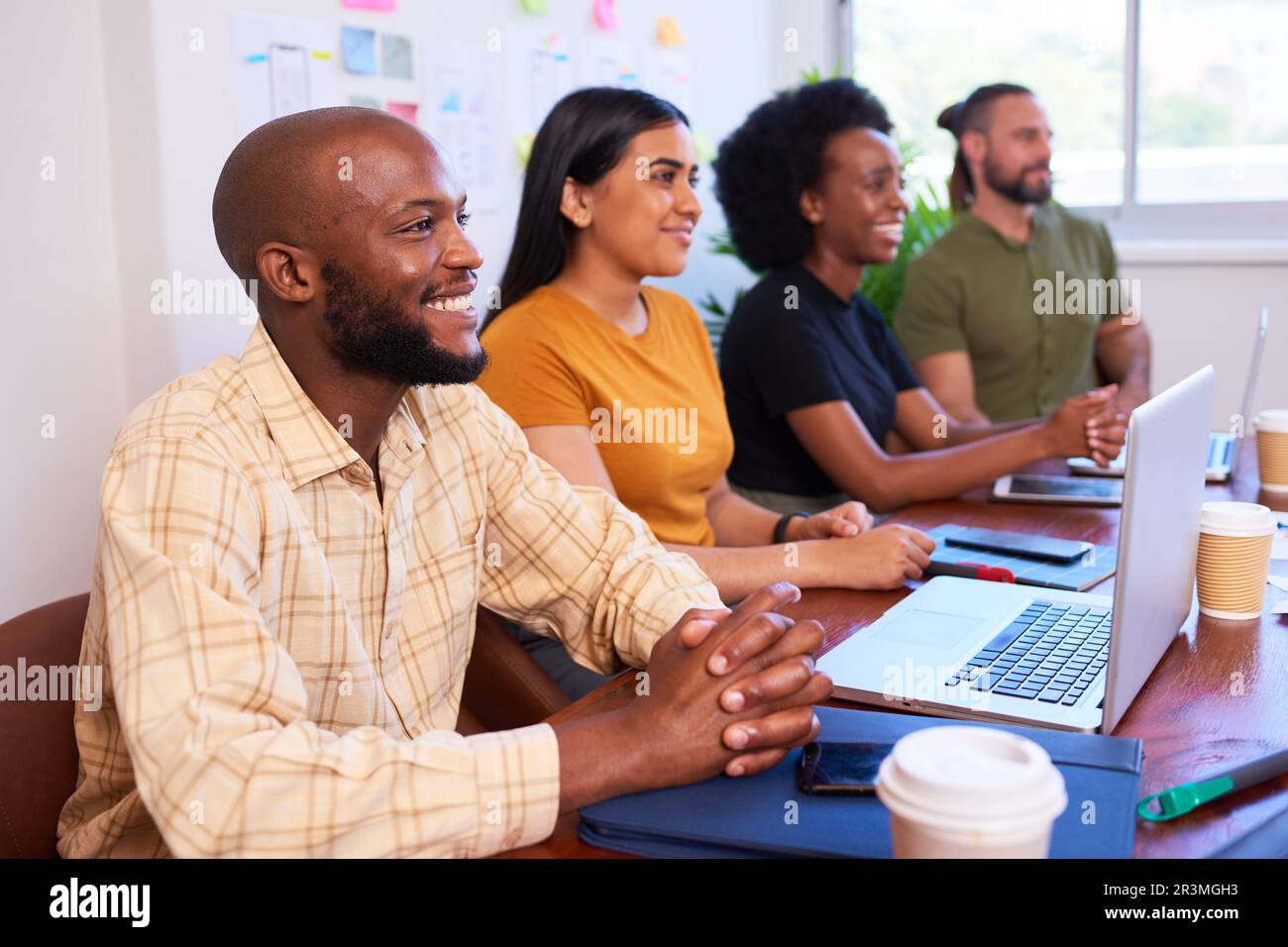 Four diverse team members sit in a row in a meeting, listening to ...