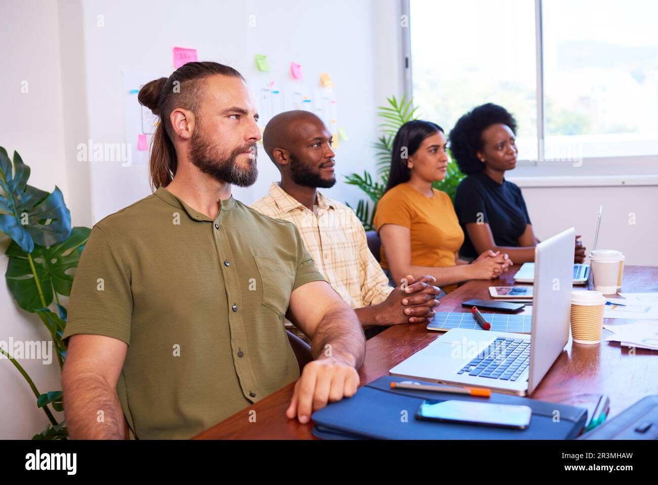 Four diverse team members sit in a row in a meeting, listening to ...
