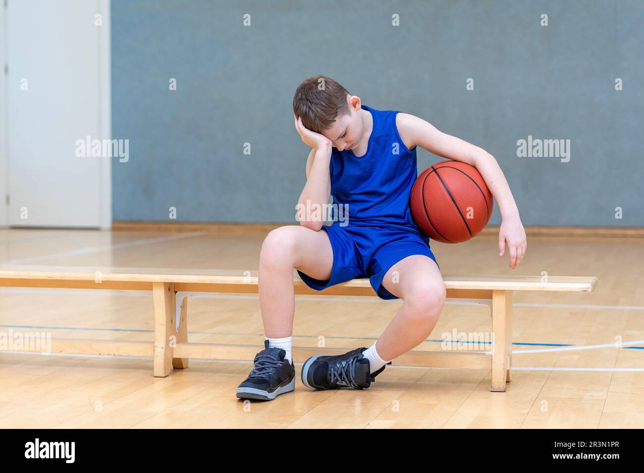 Sad disappointed boy with basketball ball in a physical education ...