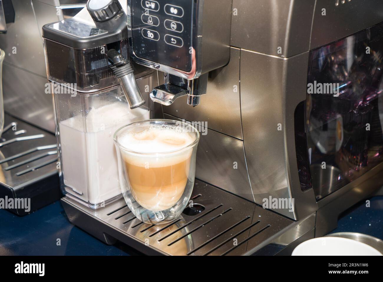 A coffee machine pours espresso into a glass cup with milk. Cappuccino ...