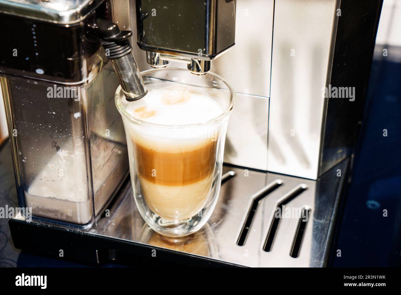 A coffee machine pours espresso into a glass cup with milk. Cappuccino ...