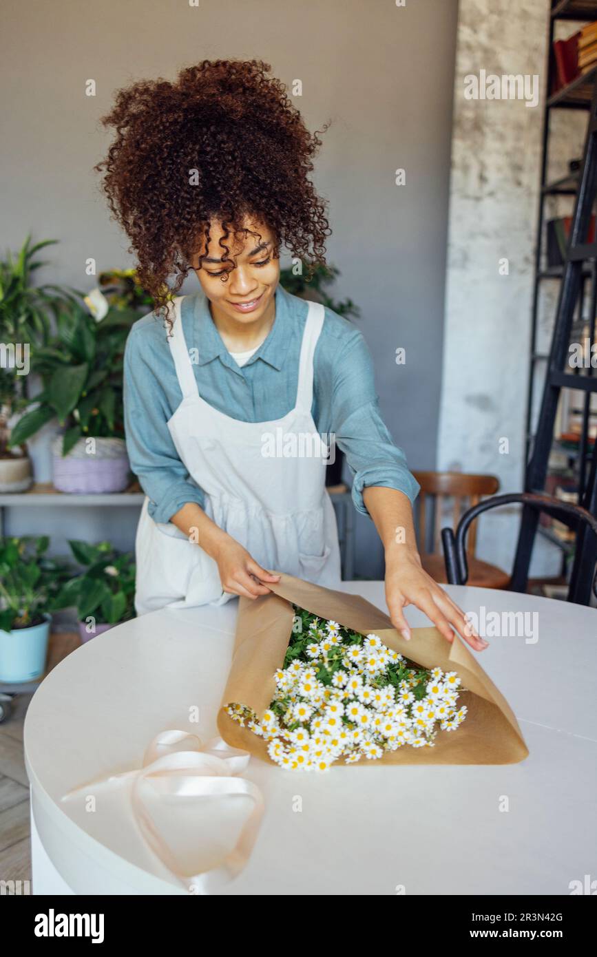 Young florist in apron creating beautiful simple daisy bouquet in craft ...